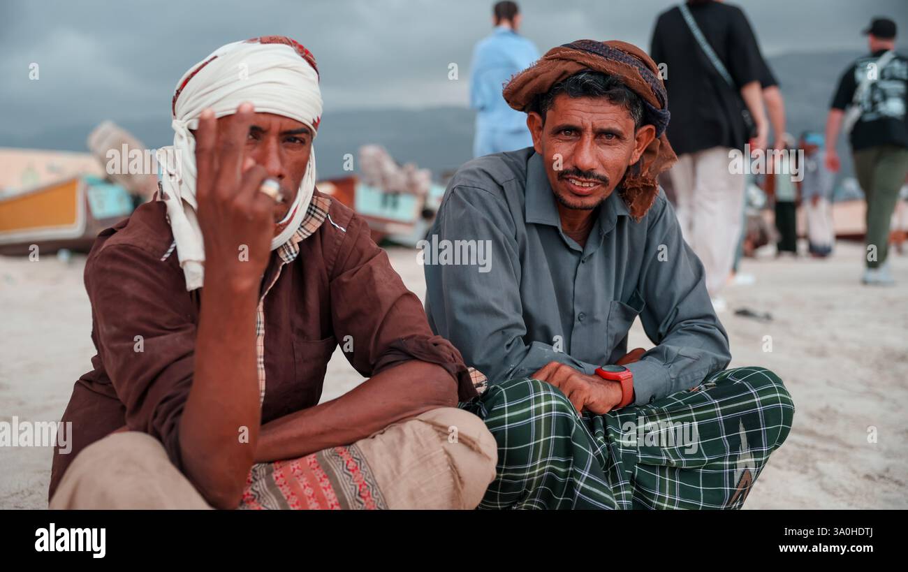 Two men sit on the sandy beach in Socotra, enjoying the warm weather ...