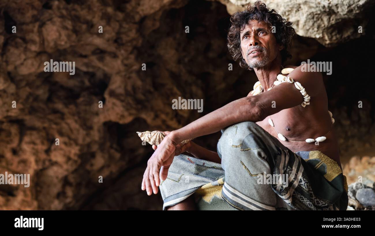 A man sits thoughtfully in a cave on Socotra, wearing traditional ...