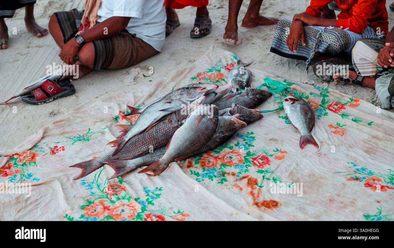 Fishermen gather around a colorful mat, showcasing their fresh catch of ...