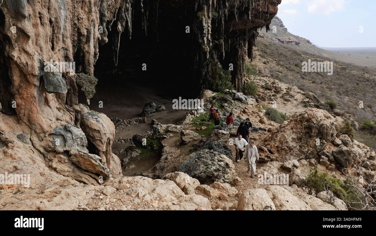 Tourists navigate rocky terrain near a cave entrance in Socotra ...