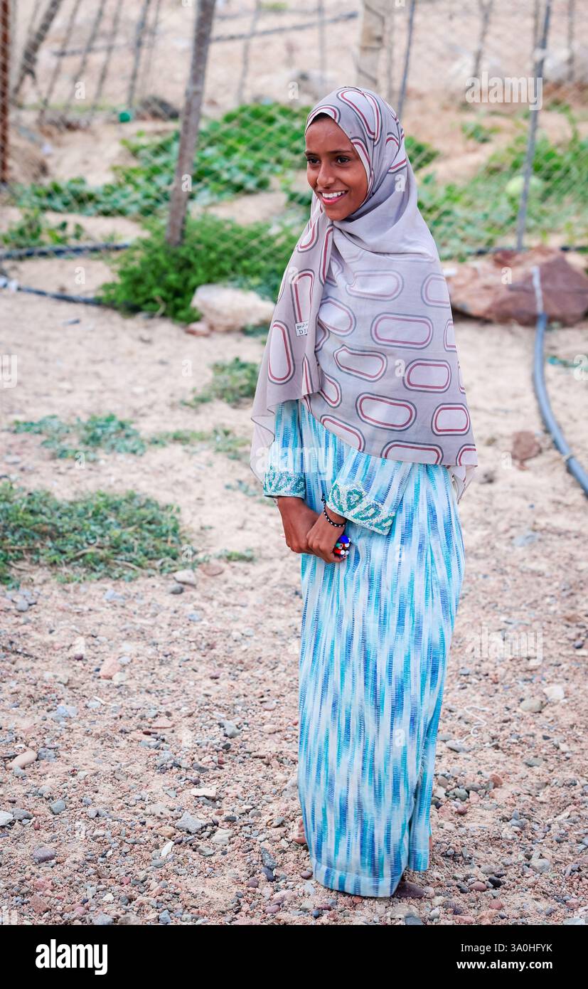 A woman wearing traditional dress smiles in a lush landscape of Socotra ...