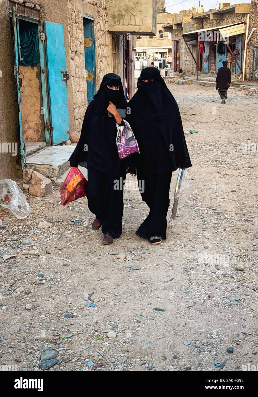 Two women in traditional attire stroll through a dusty street in ...