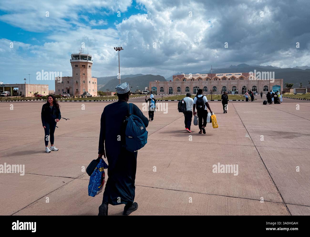 A group of travelers walks towards Socotra Airport, with clouds ...