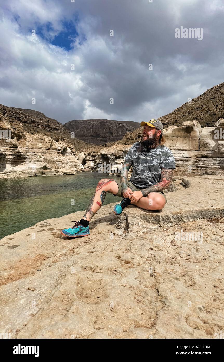 Tourist sits on a rock near clear waters in Socotra, surrounded by ...