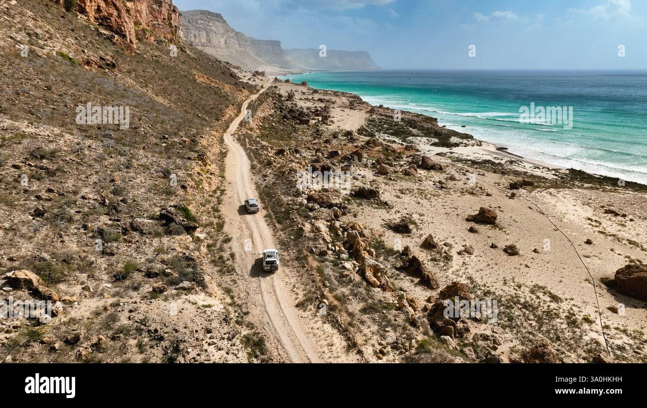 Two vehicles traverse a sandy track along the stunning coastline of ...