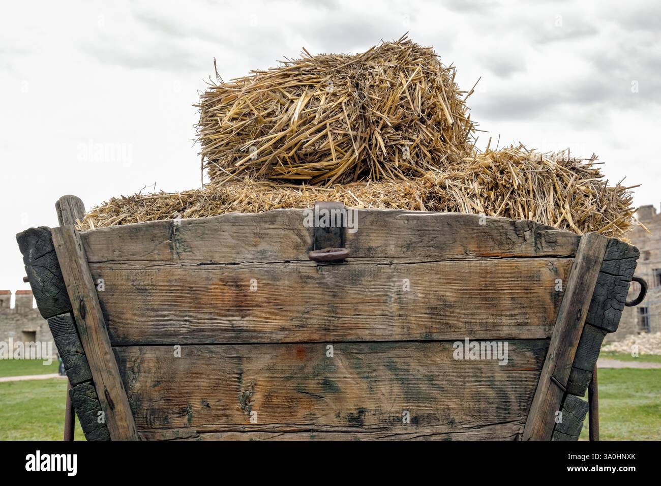 Old wooden cart with bales of hay against background of stone walls of ...