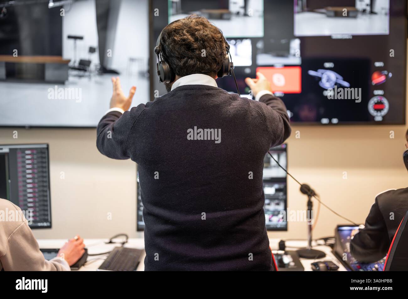 A television director in a broadcast control room, actively guiding a ...