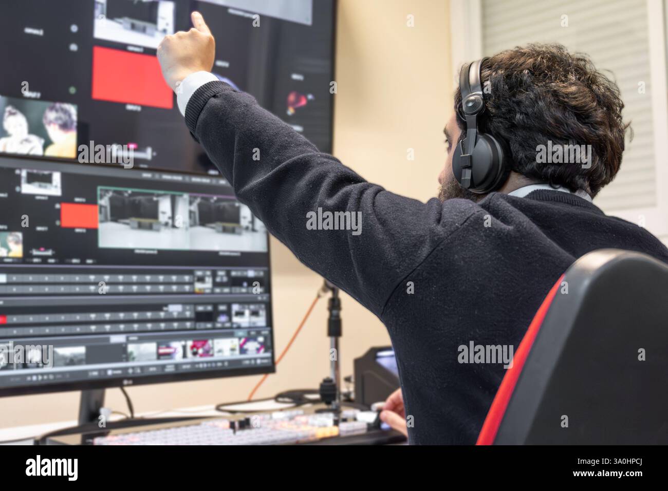 A television director in a broadcast control room, actively guiding a ...