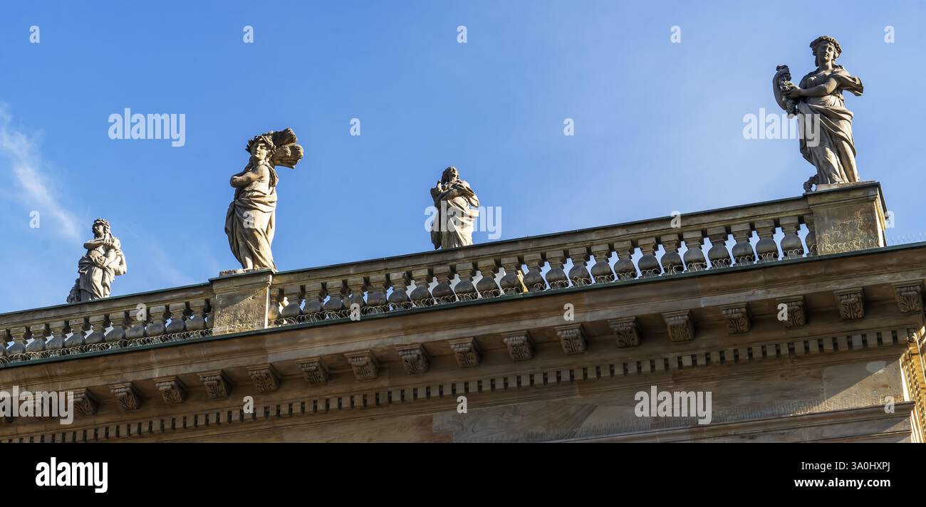 Four classical statues atop a historic building against a clear blue ...
