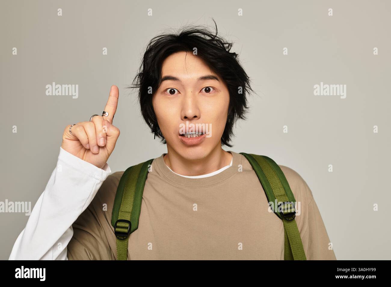 Stylish young Asian man playfully raises a finger in a chic setting ...