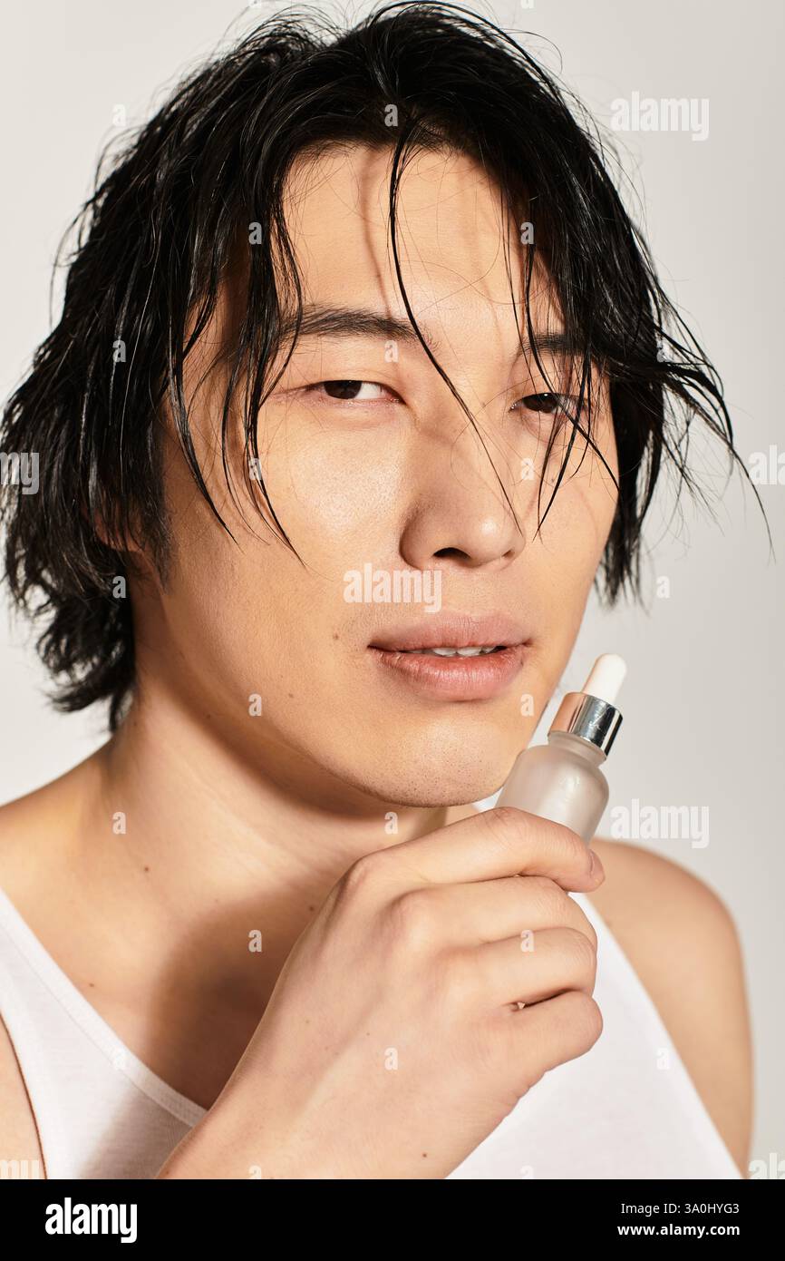 Young asian man confidently poses with skincare serum, radiating modern elegance and urban flair ...