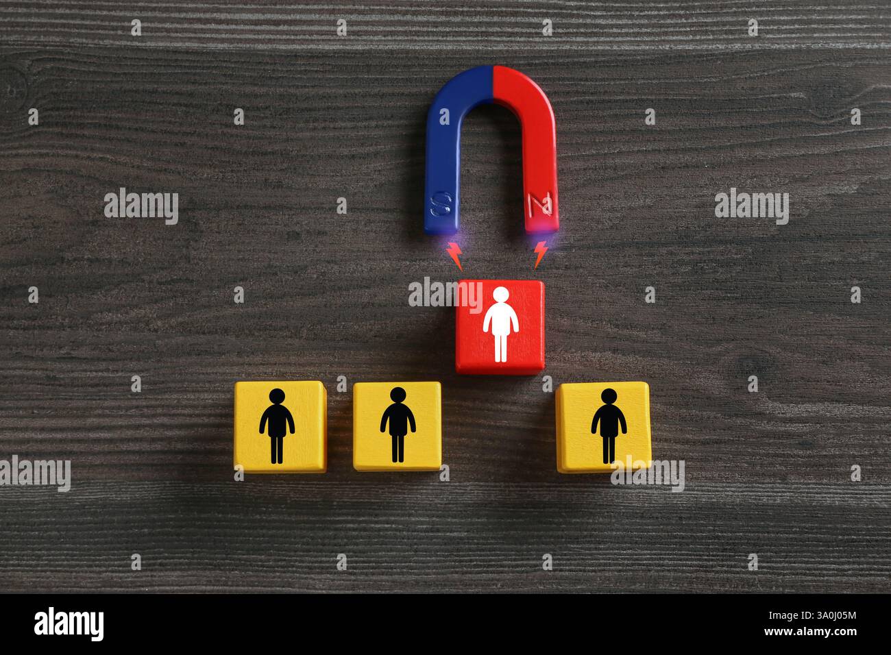 Magnet attracting one of cubes with human figures on wooden background ...