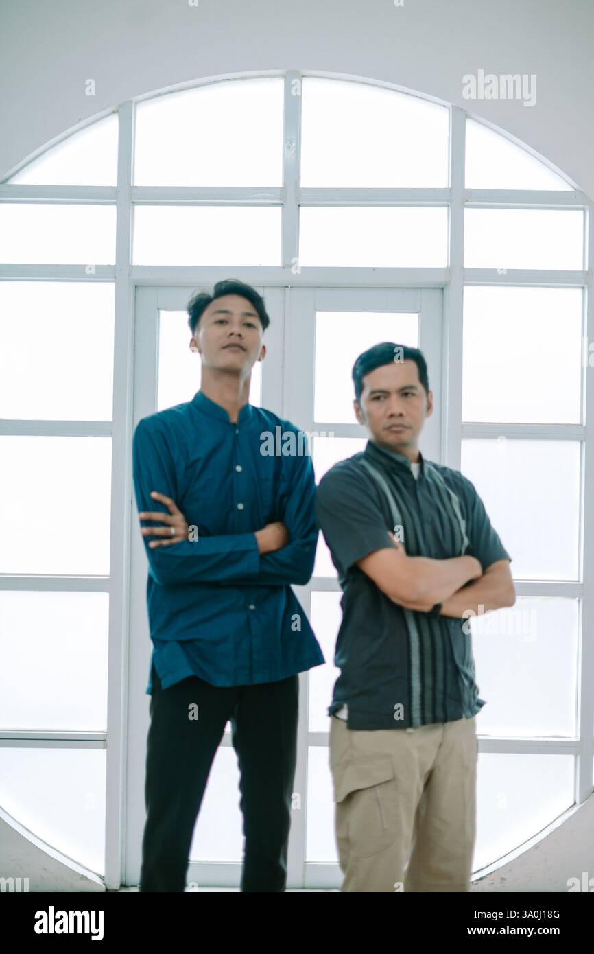 Two Asian men standing confidently indoors near a window with their ...