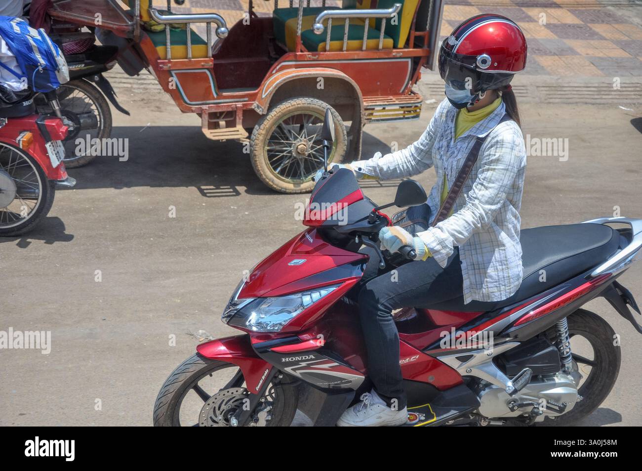 Phnom Penh, Cambodia - May 6, 2009: Woman rides a red scooter past a ...