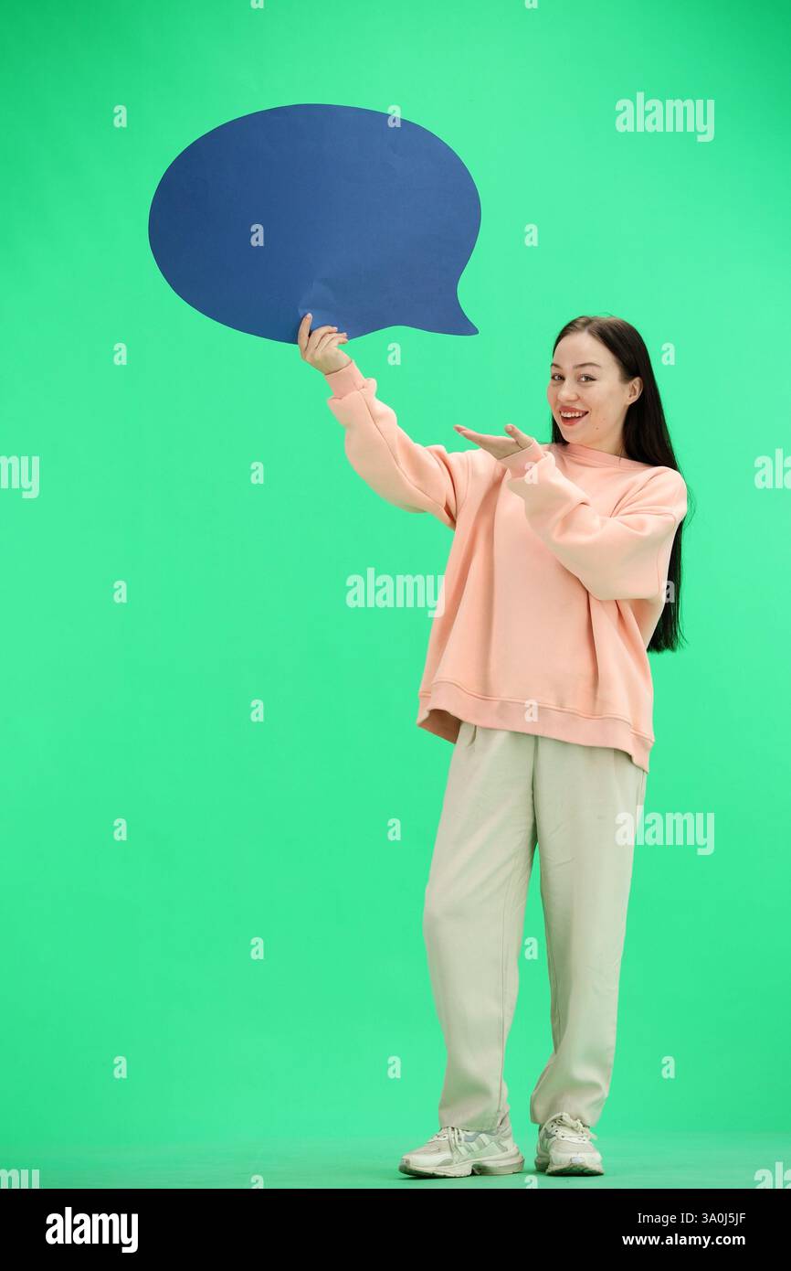 A woman, full-length, on a green background, with a blue comment mark ...