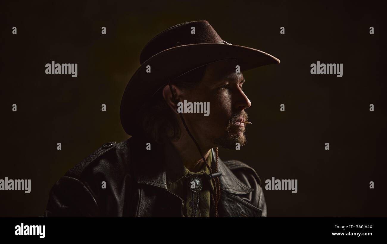 Thoughtful man, cowboy in leather coat and hat, smoking cigarette ...