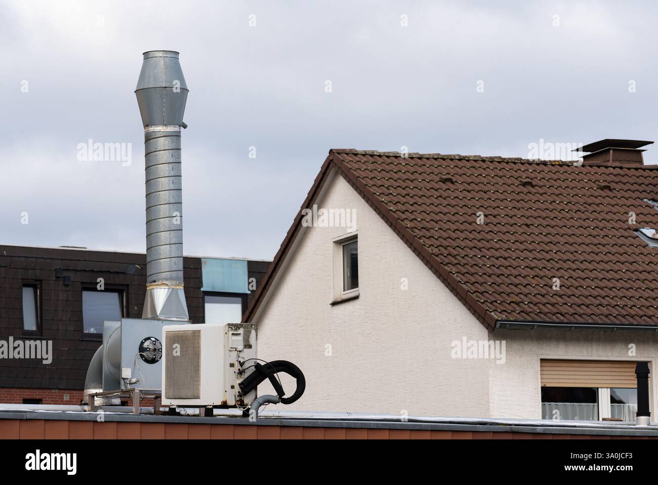 A metal air vent system rises above the rooftop of a suburban building ...