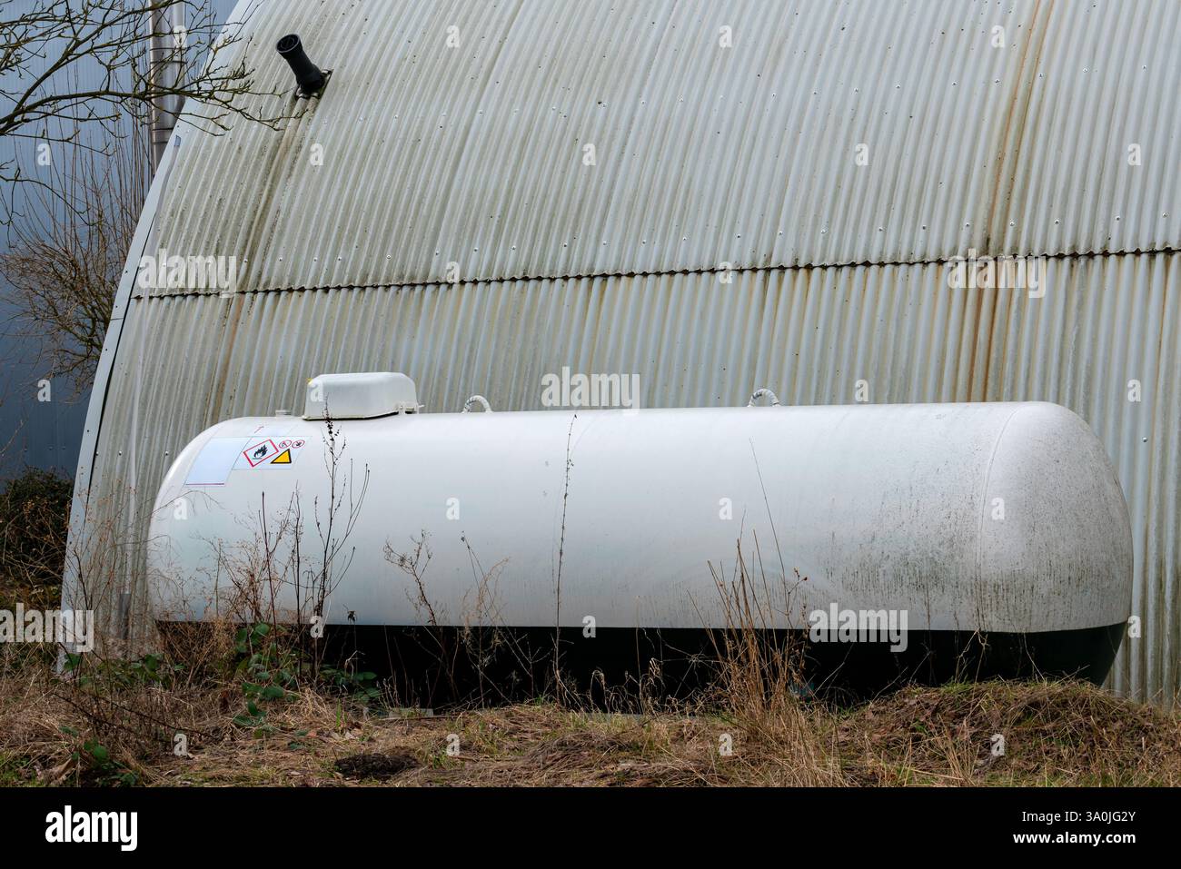 A white storage tank rests next to a corrugated metal building ...