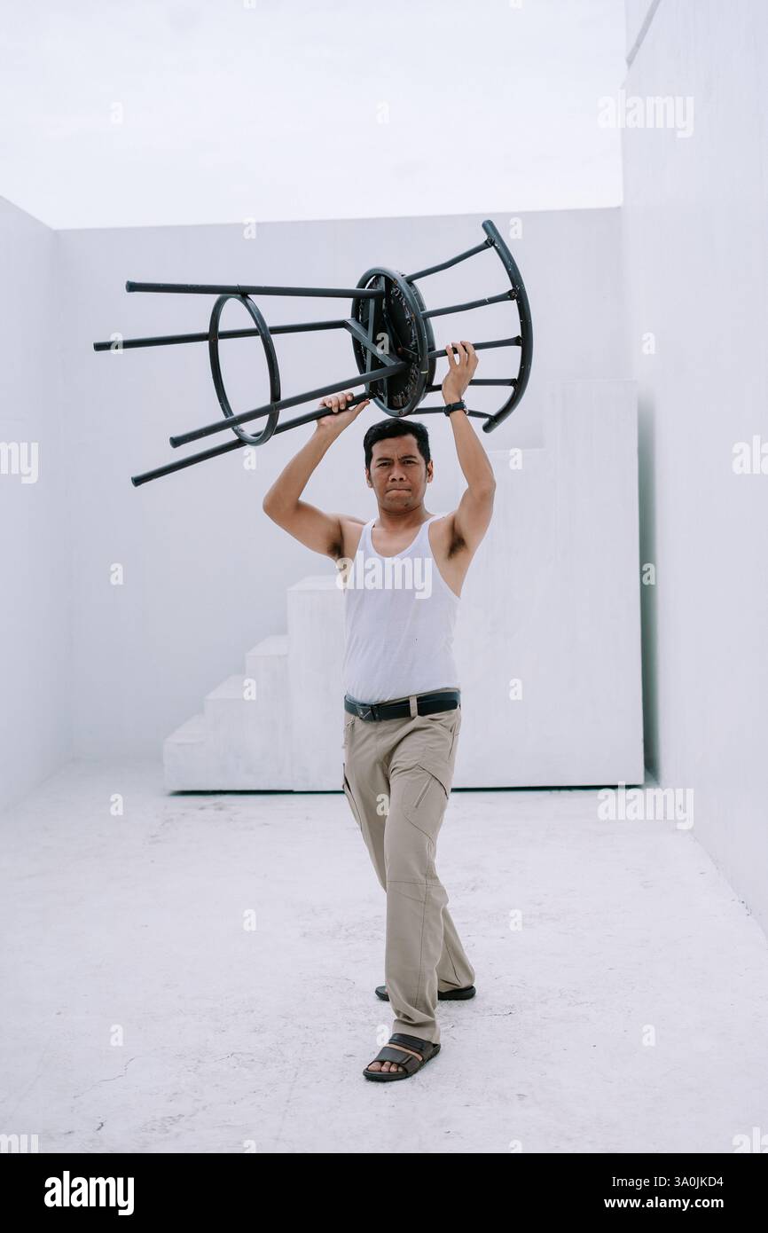 An Asian man in casual clothes is lifting up a black metal chair ...