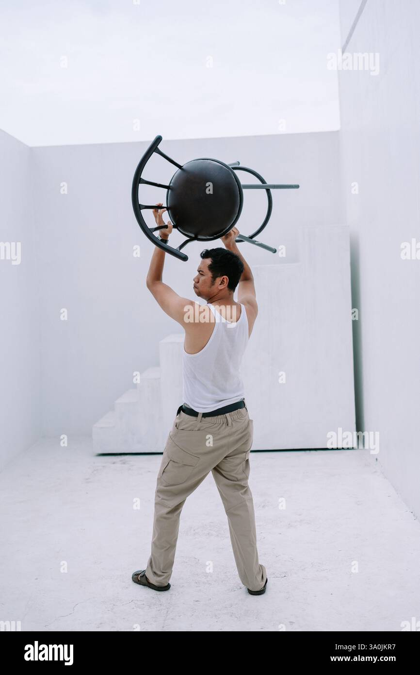 A man lifts a metal chair overhead demonstrating physical strength in a ...