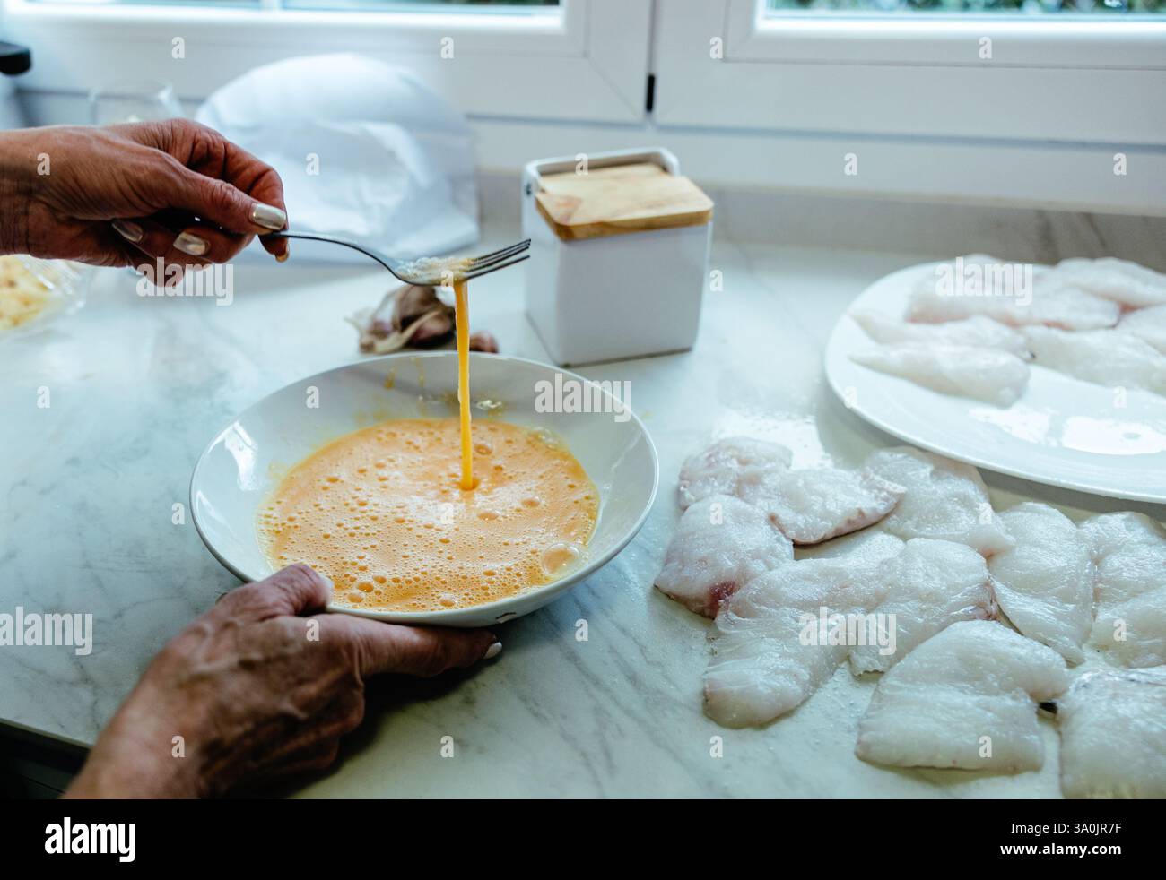 Close-up of a person mixing beaten eggs with a fork next to fresh raw ...