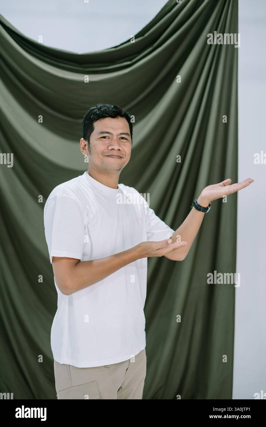 A smiling man in a white t-shirt is presenting or introducing something ...