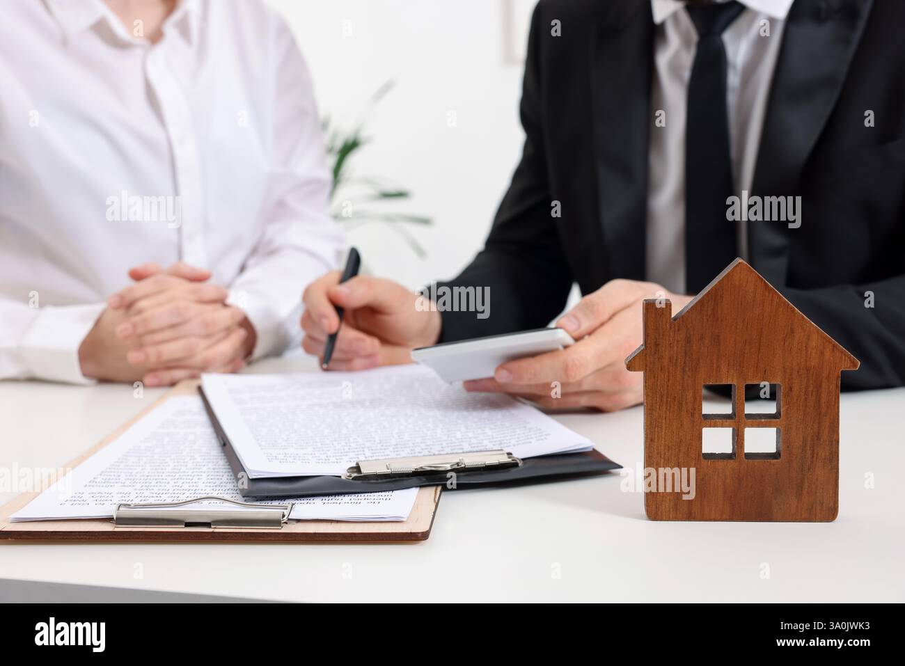 Real estate agent showing client where to sign document at white table ...