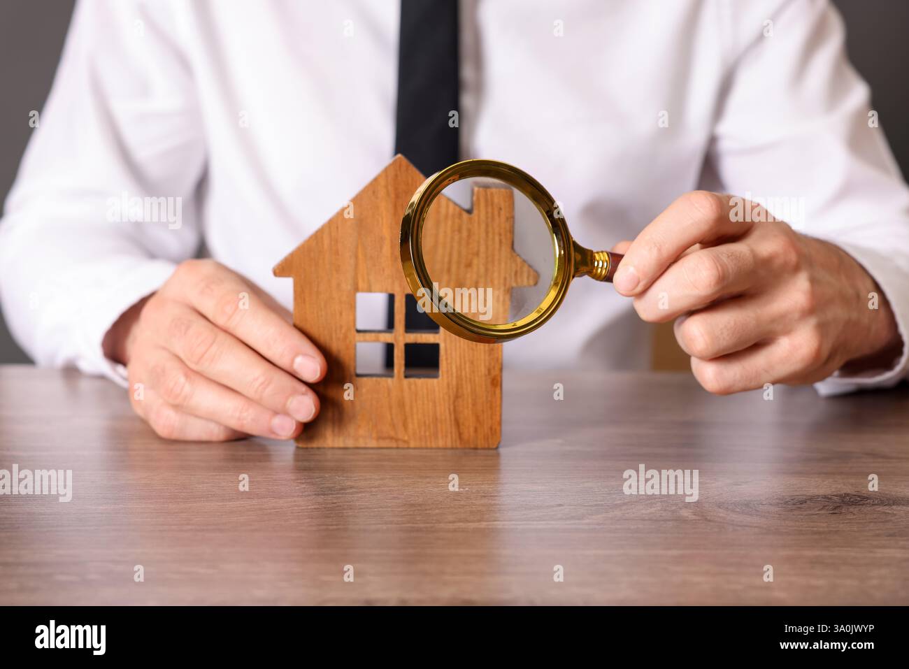 Real estate agent with house figure and magnifying glass at wooden ...