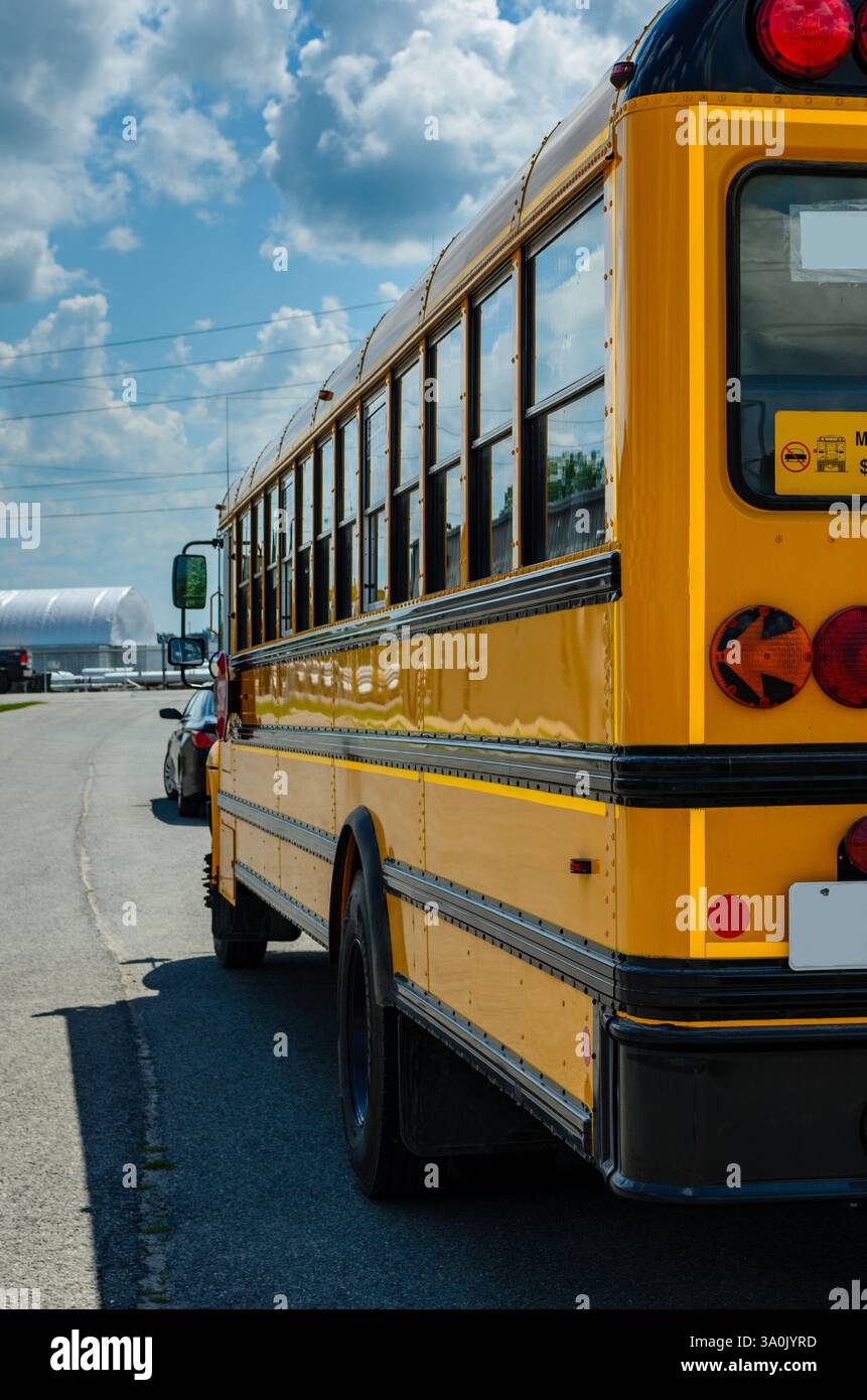 Rear left view of a school bus behind a car under a cludy blue sky ...