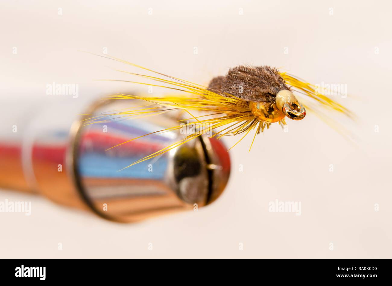 Macro front view of a single yellow fishing fly in a vise against a ...
