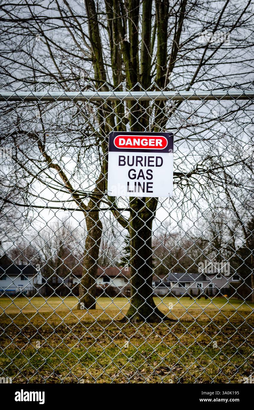 Buried Gas Line sign on a park chain-link fence with trees and houses ...