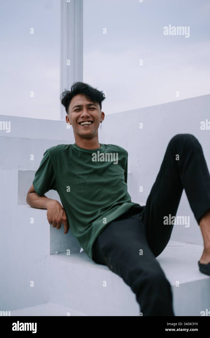 A cheerful young man relaxes on bright white steps, his radiant smile ...