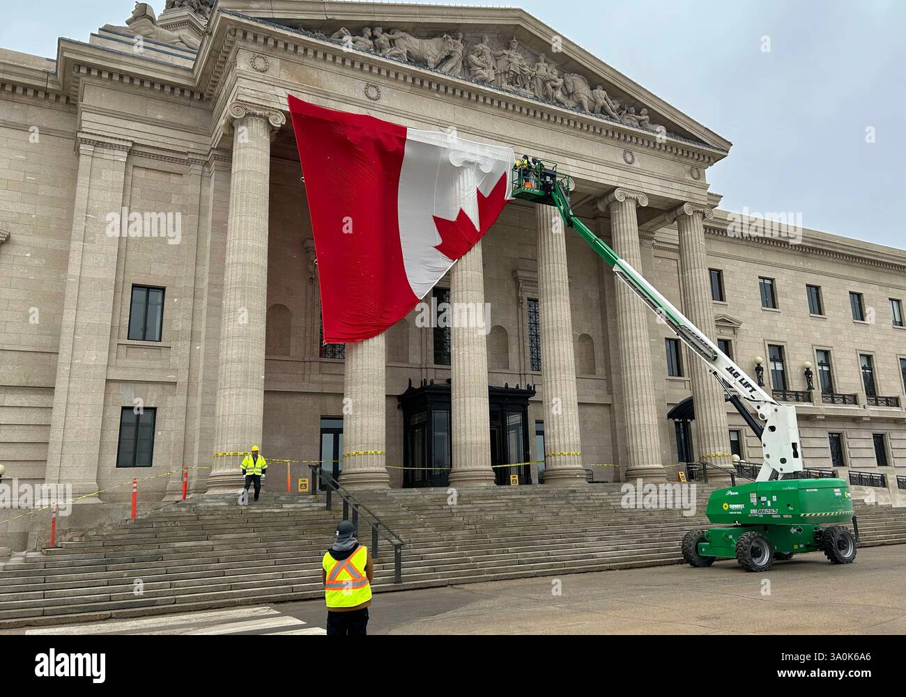 Workers install a large Canadian flag on the front of the Manitoba ...