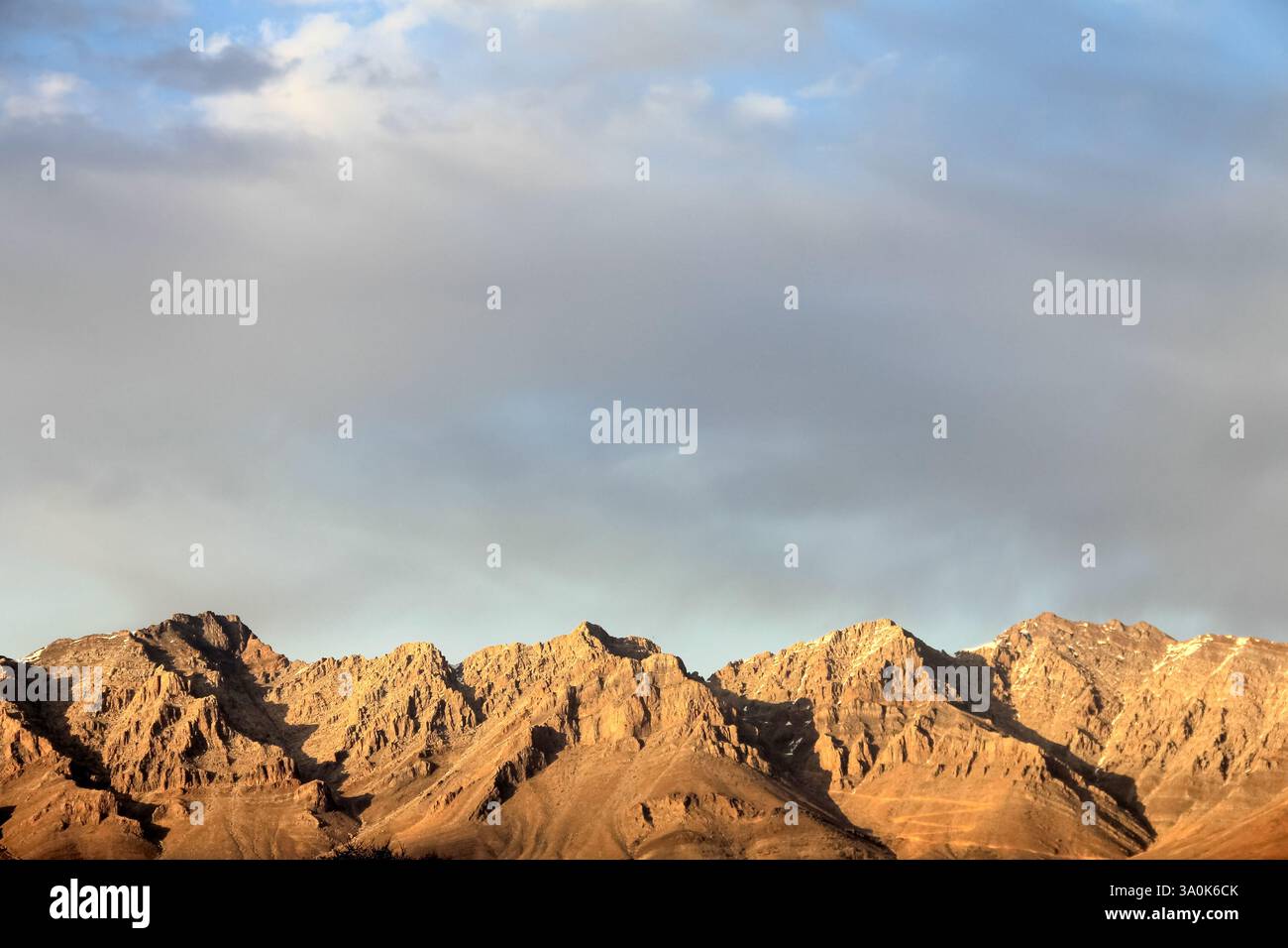 A view of a rugged mountain range under a calm blue sky. The warm ...