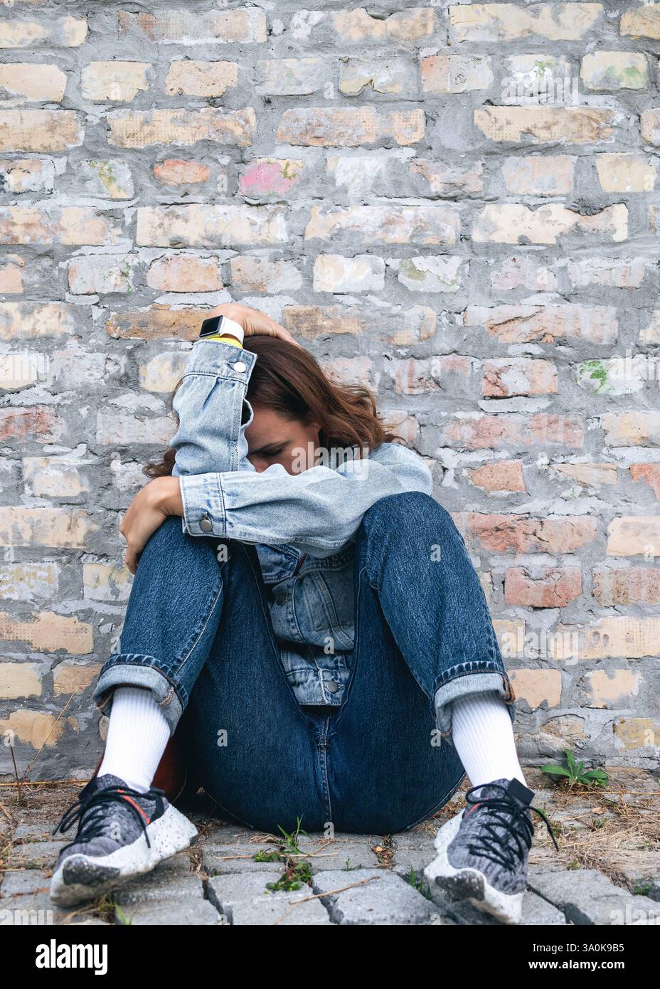 Depressed woman curling up sitting on the ground next brick wall Stock ...