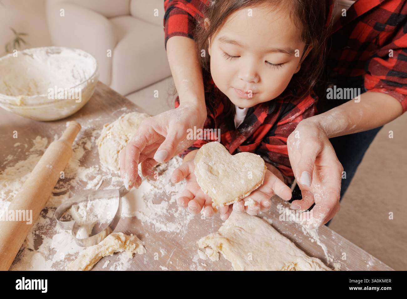 Mother and child baking together, hands holding heart-shaped dough ...