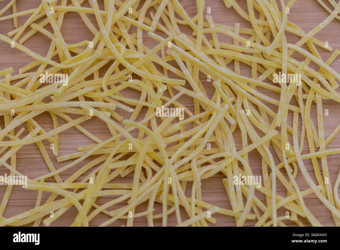 A close-up of yellow spaghetti pasta noodles on top of a table, a pile ...