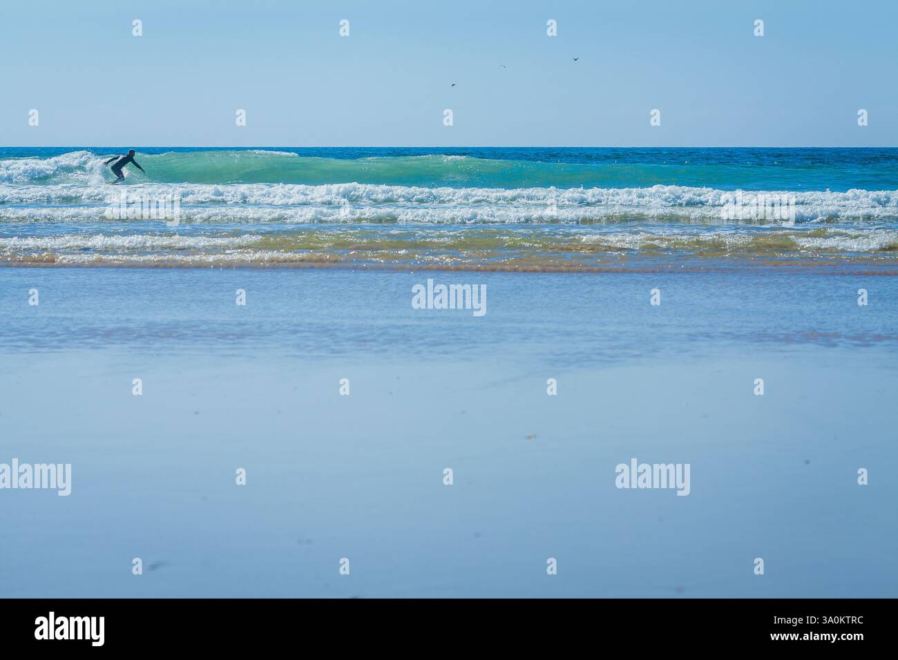 This image captures a surfer riding a gentle wave along the shoreline ...