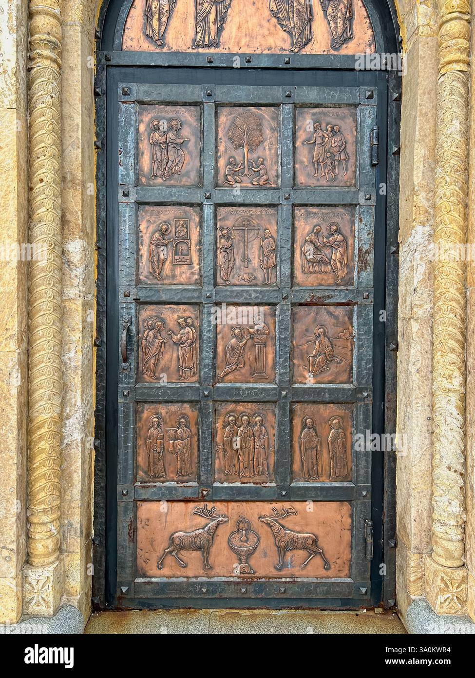 This image shows an ornate bronze church door with engraved religious ...