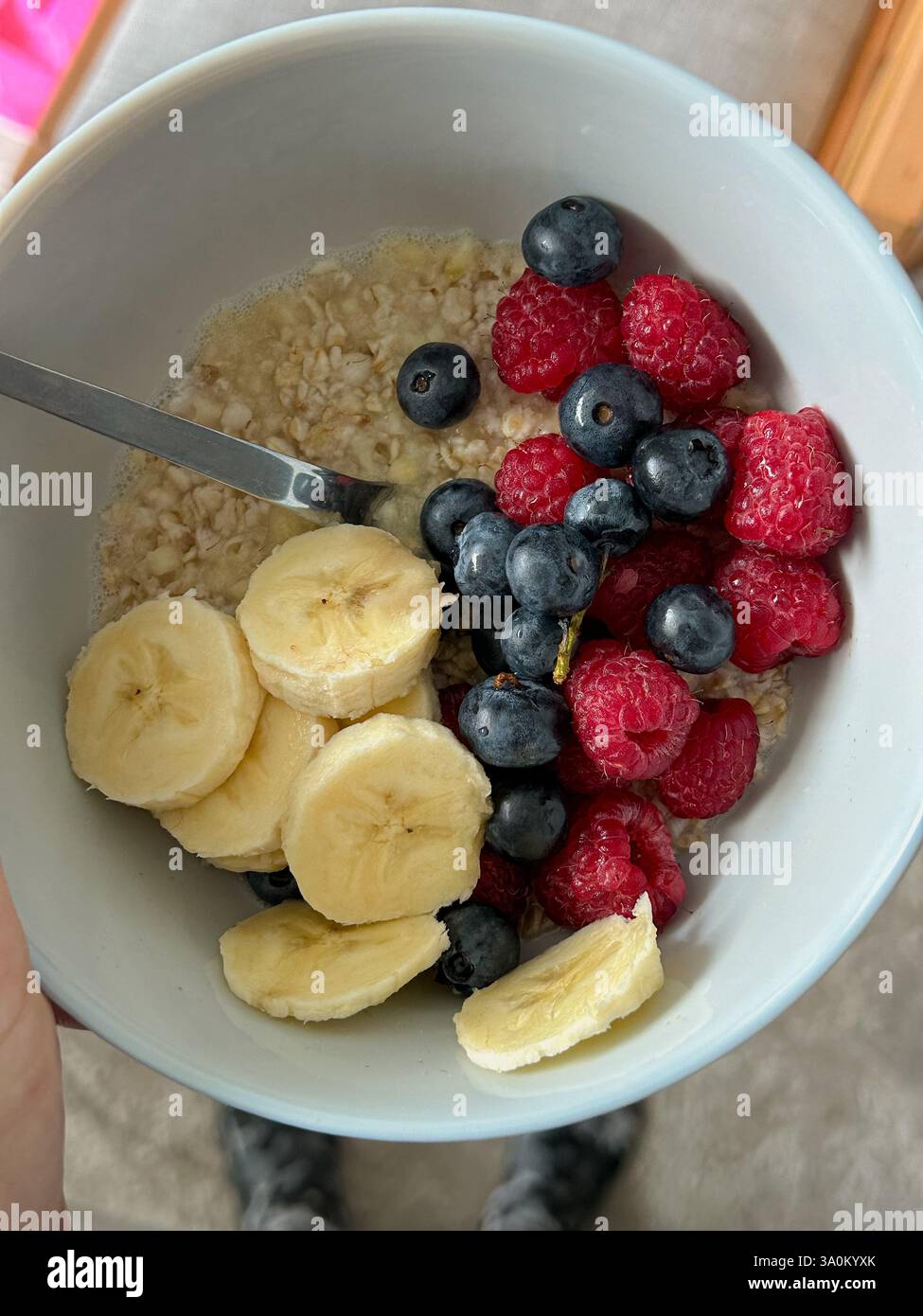 A white bowl contains oatmeal topped with banana slices, raspberries ...