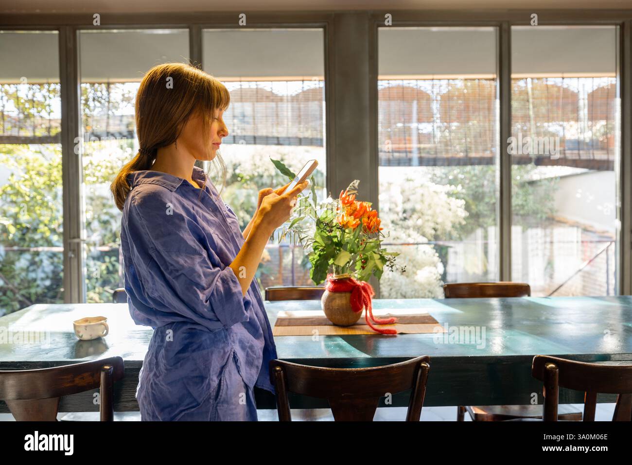 A barefoot woman in a relaxed blue outfit stands by a rustic dining ...