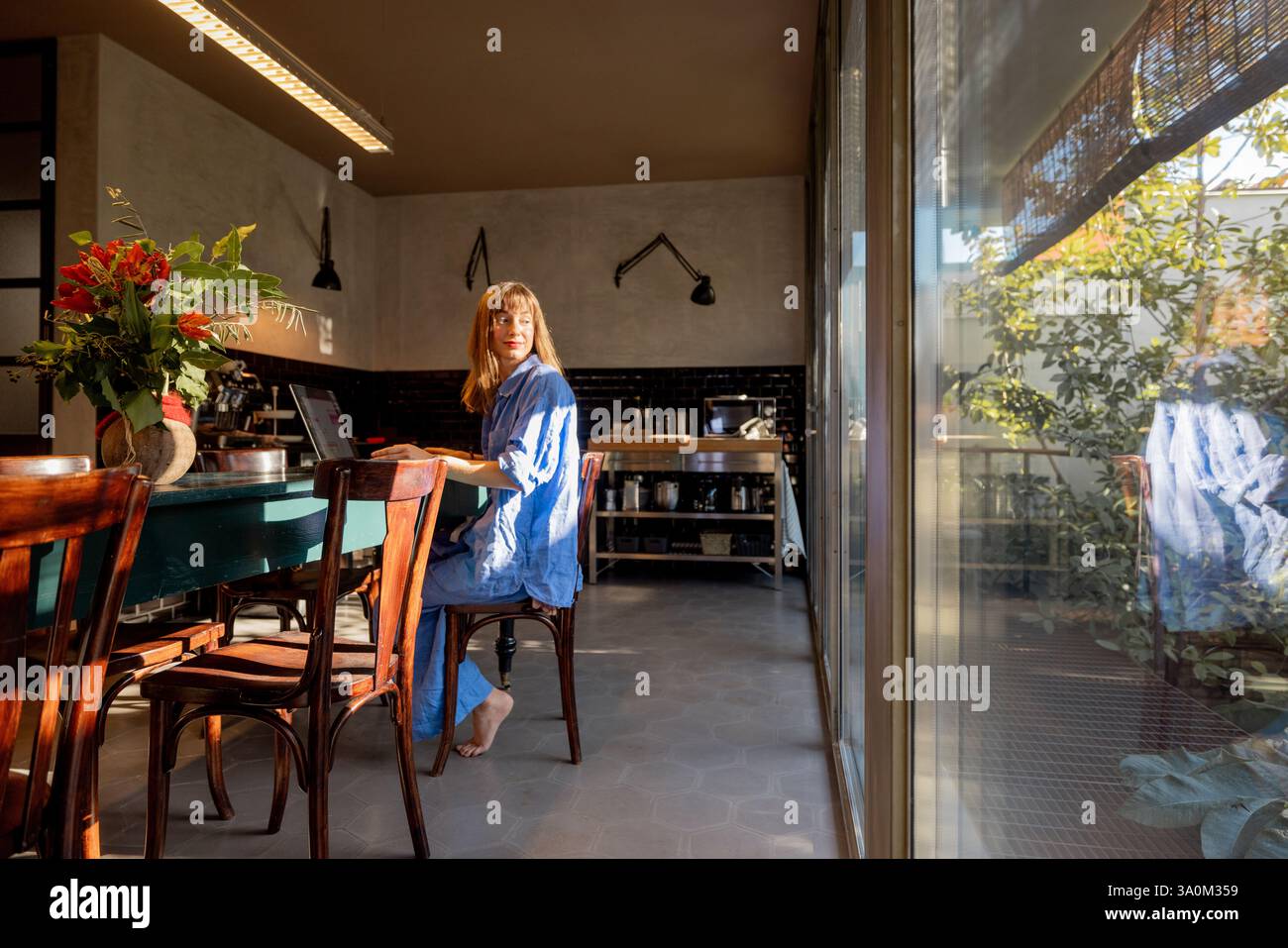 A barefoot woman in a relaxed blue outfit works on her laptop at a ...