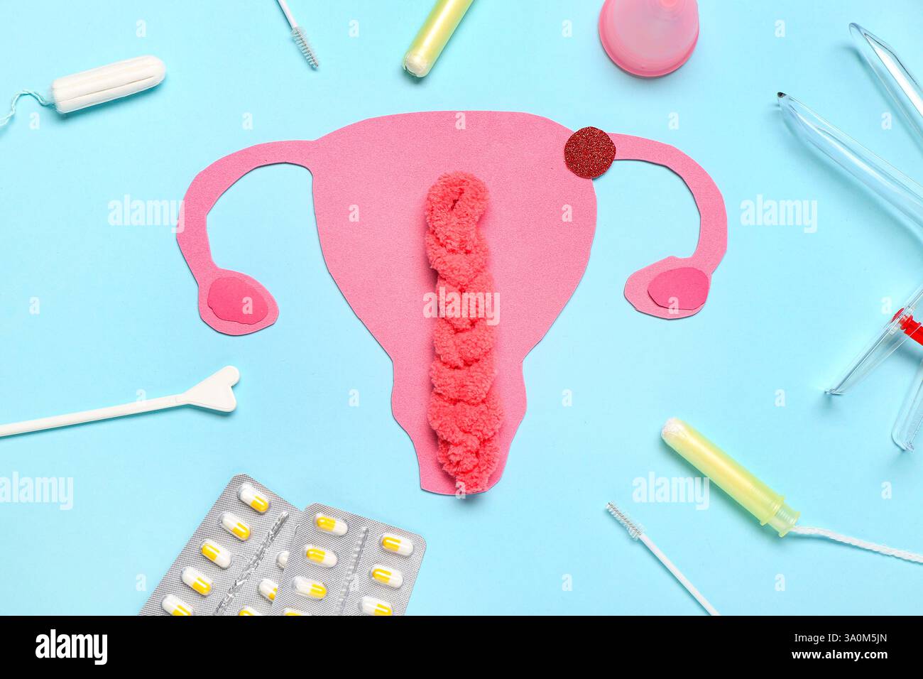 Paper uterus with gynecological speculum, pills and tampons on blue ...