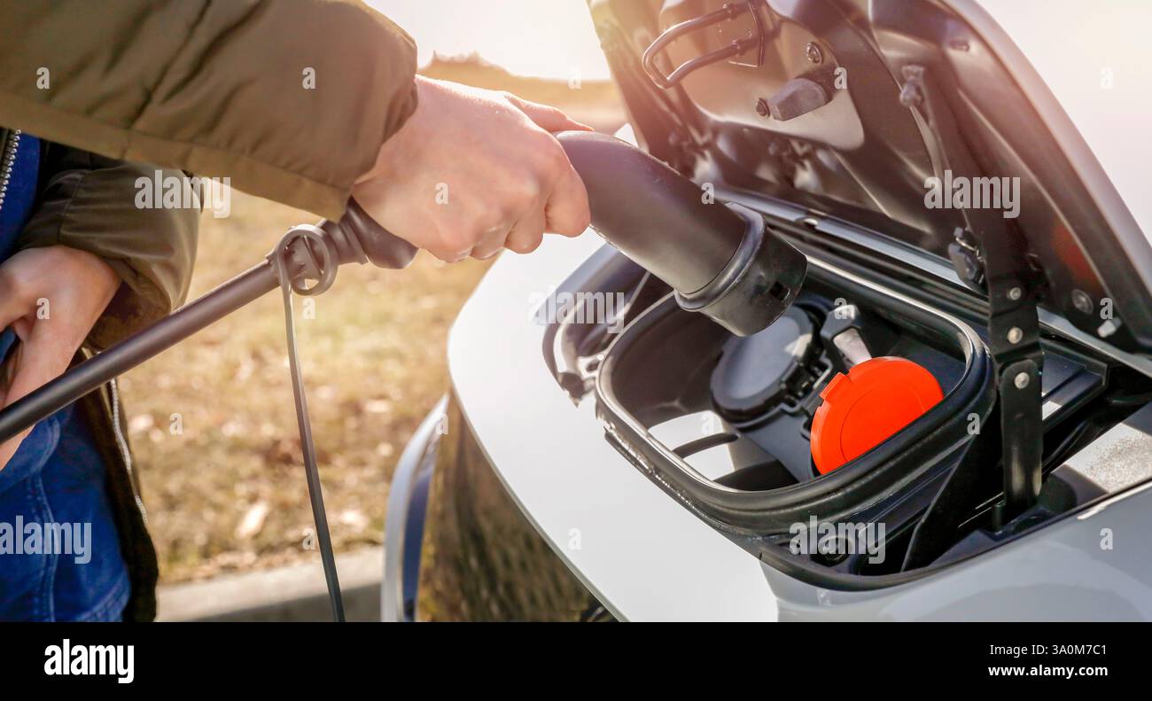 Close-up of an electric car's charging port with a hand plugging in a ...