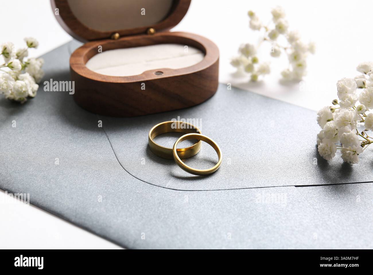 Wedding rings on envelope with flowers and wooden box on white ...