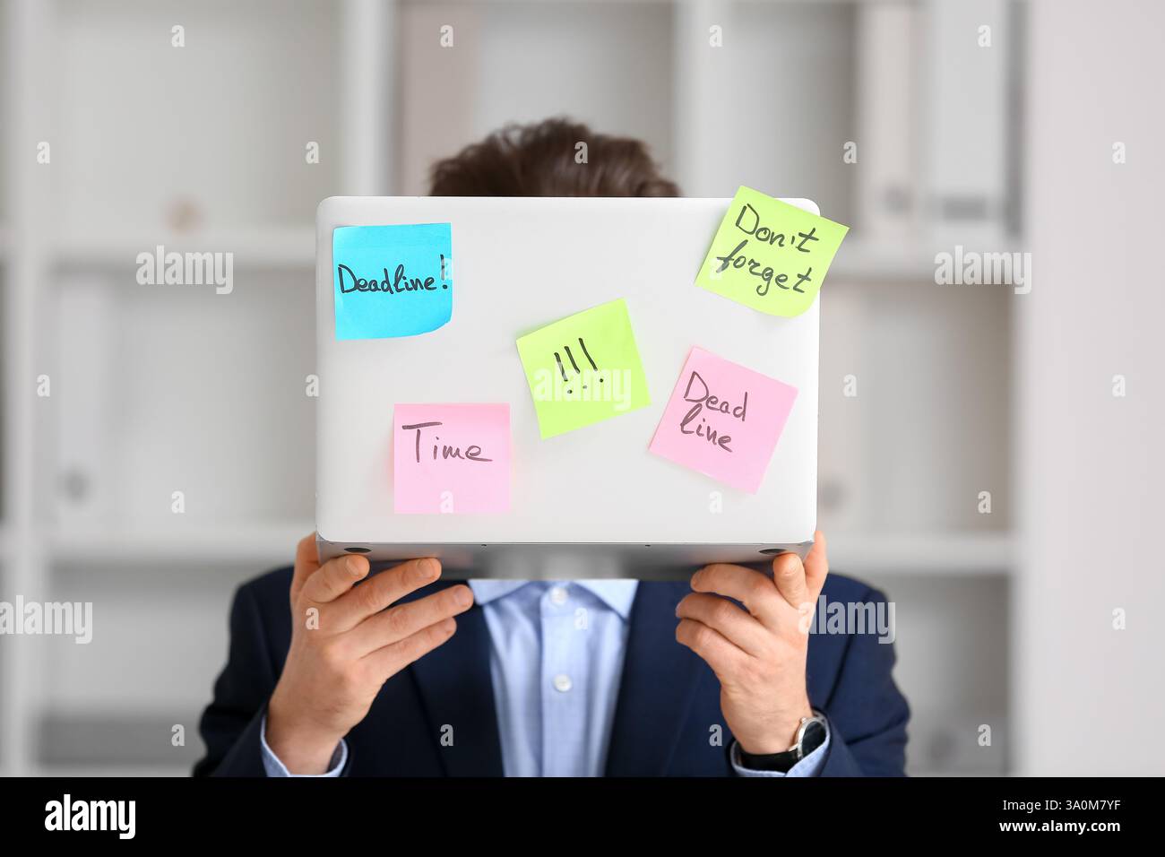Stressed businessman hiding his face behind laptop in office. Deadline ...