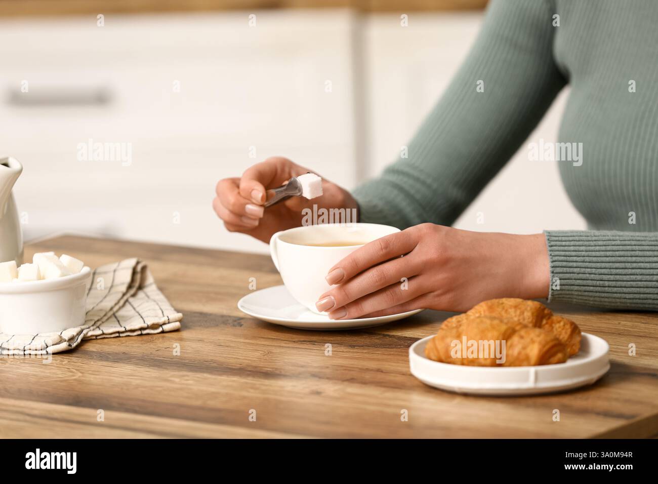 Woman adding lump of sugar into tea at table in kitchen. Closeup Stock ...