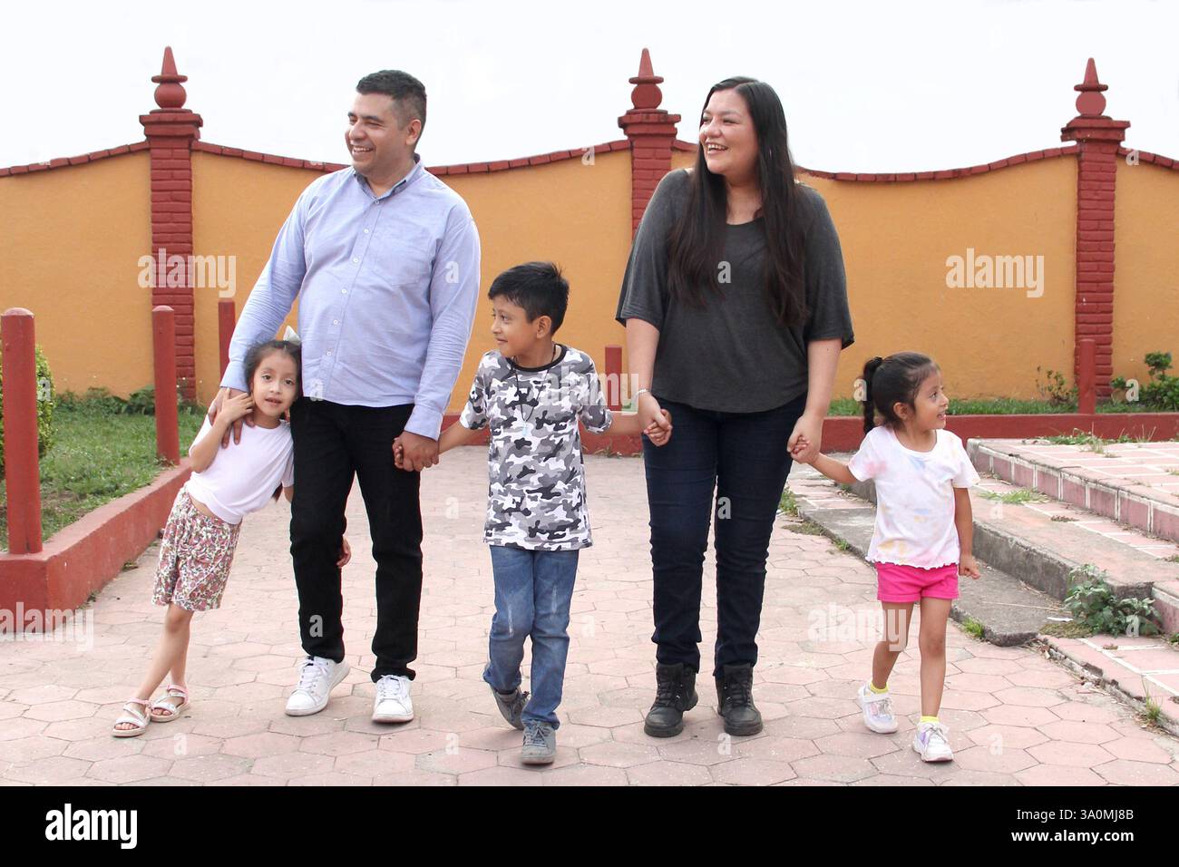 Brunette Latin family of dad, mom, daughters and son walk in the park ...