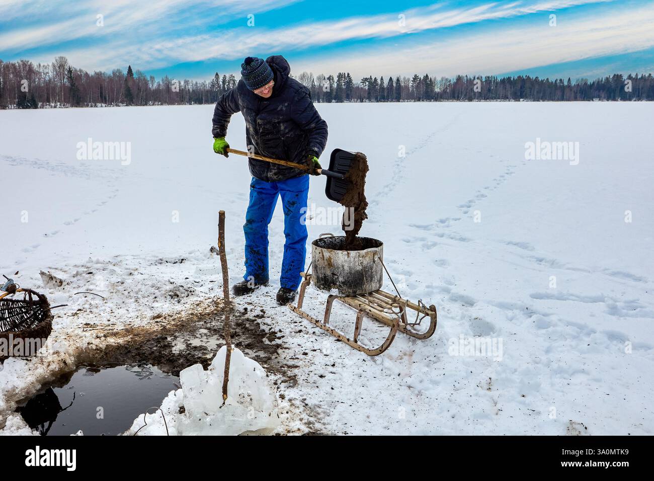 Farmer mines sapropel freshwater sediments by pulling basket of lake ...