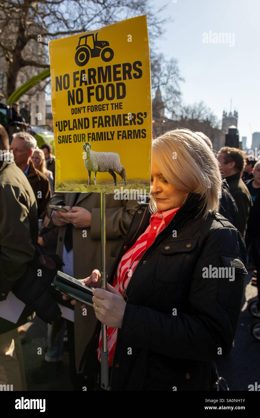 A protester looks on her phone as she holds a placard expressing her ...